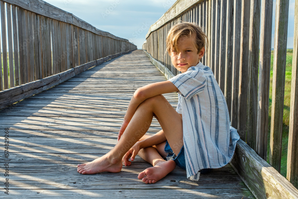 Foto stock di Young Preteen Boy Sitting on Sunny Boardwalk Wearing ...