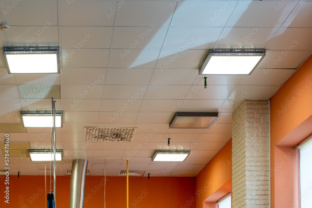 Square fluorescent lamps on the ceiling. Thick pipes of the air ...