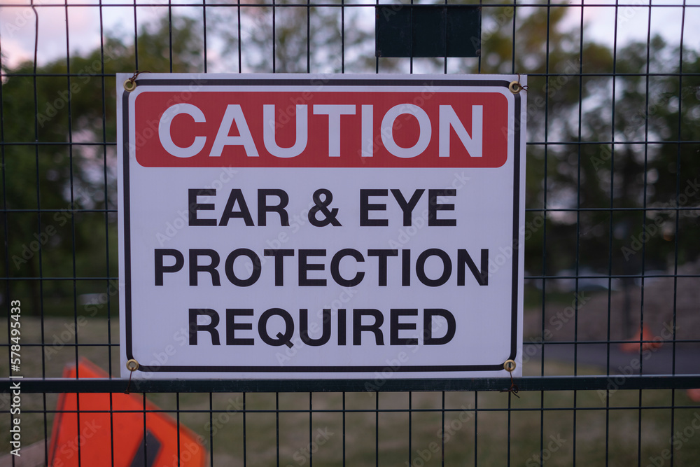 Sign caution ear and eye protection required on the metal fence at ...