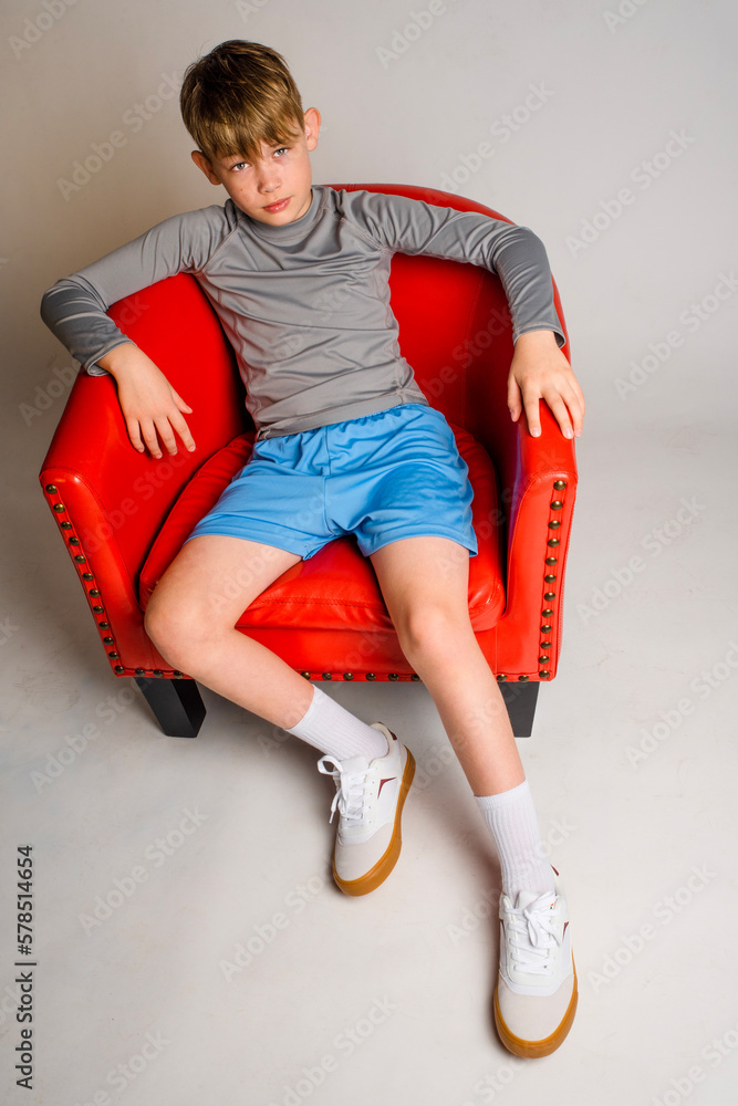 Preteen boy casually sitting waiting in a red chair Stock Photo | Adobe ...