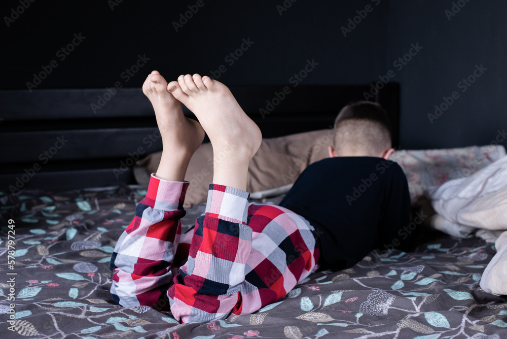 A child with bare feet is lying on a bed. Leg and foot. A child in ...
