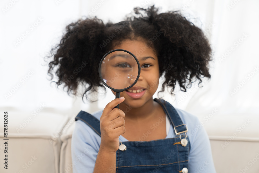 Smiling child girl playing magnifying in classroom. African American ...
