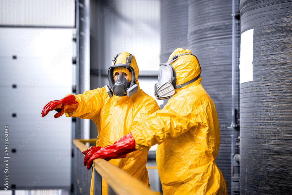 Factory worker standing by large metal storage tanks with acids wearing ...