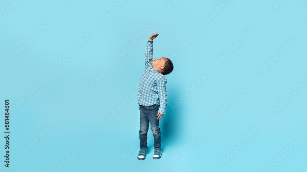 Little african american boy wishes he were taller, raising his hand to ...