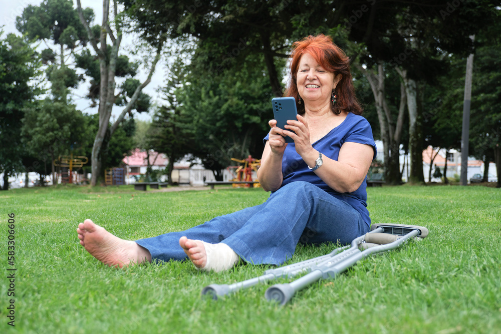 Mature latin woman resting on the grass, smiling while using her ...