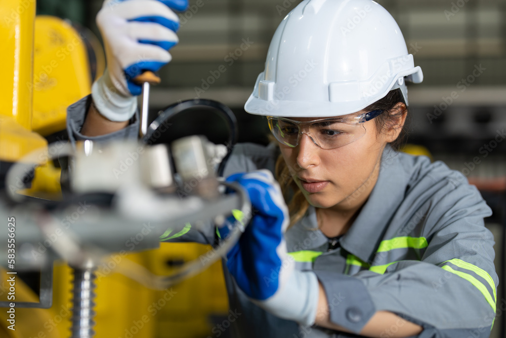 Female engineer checking and maintaining robot arms machine at factory. Technician woman in ...
