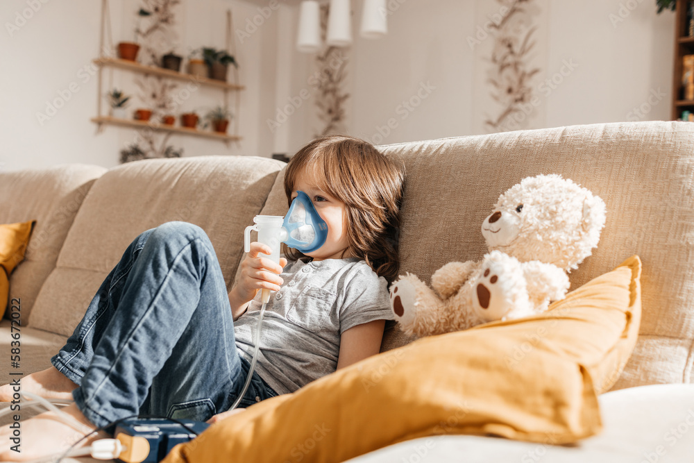 Little boy makes inhalation with a nebulizer at home lying on the couch ...