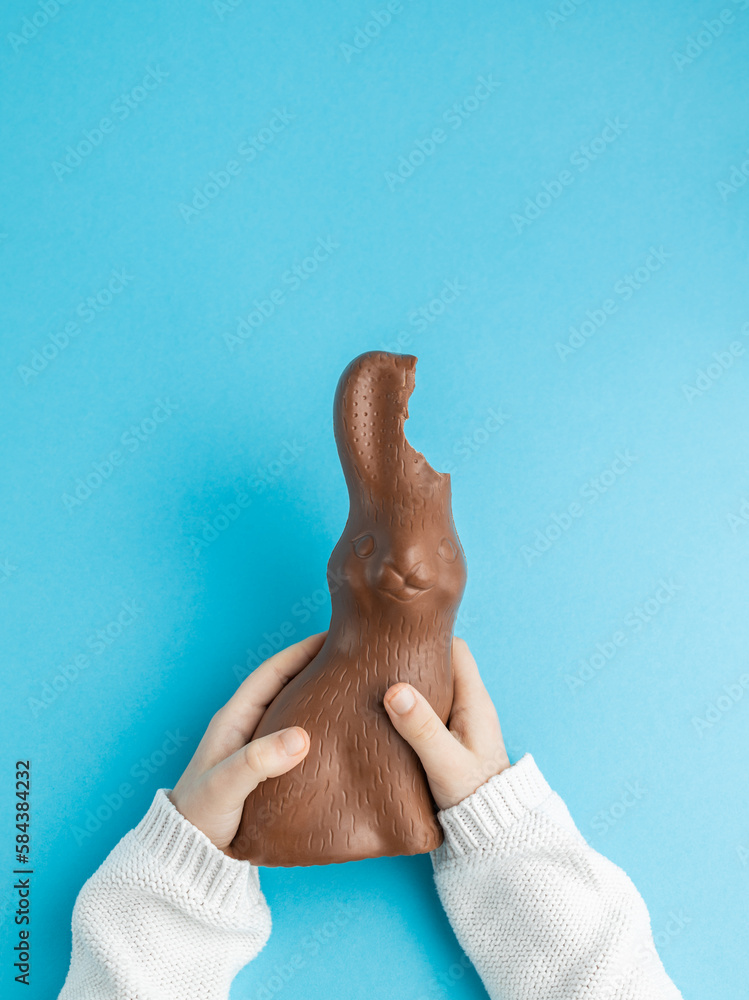 Chocolate Easter bunny with ears bitten off in hands of child on blue ...