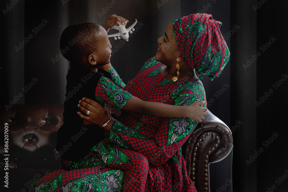 African son showing his plane toy to his mom, woman in traditional ...