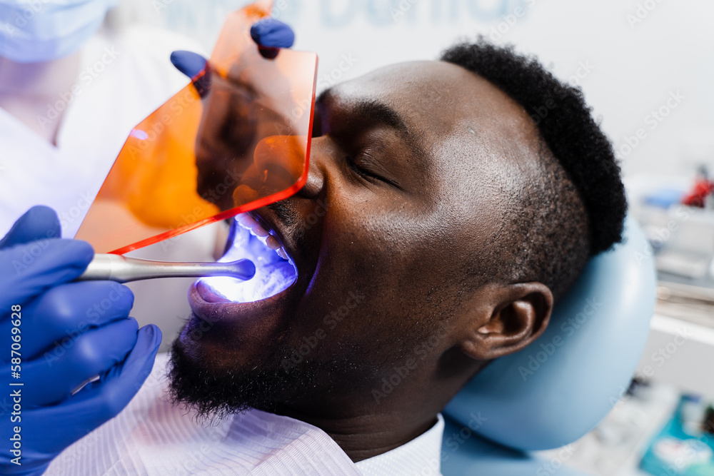 Dentist treats and removes caries in african man patient. Uv ...
