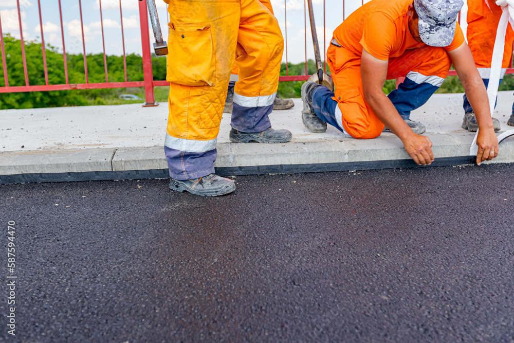 Workers apply black bitumen membrane strips for waterproofing roads and ...