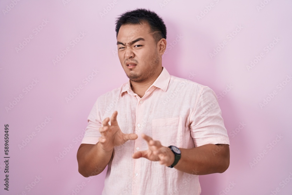 Chinese young man standing over pink background disgusted expression ...