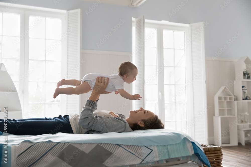 Cheerful young new mom holding kid, lifting sweet positive baby up in ...