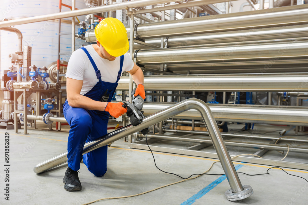 Factory worker in yellow hard hat operate with stainless steel pipe ...