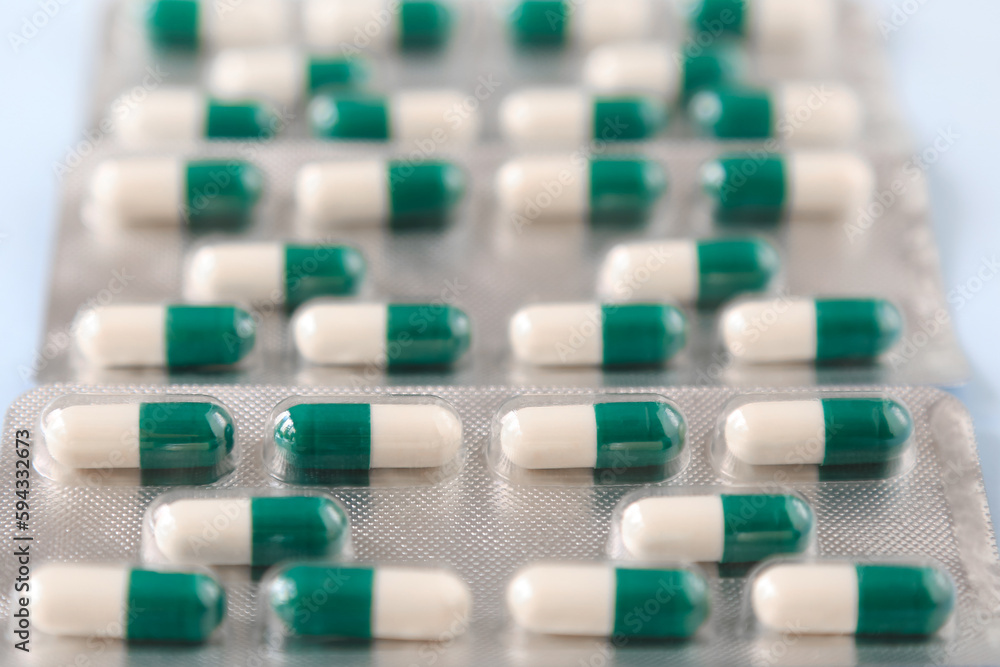 Green and white medical pills in aluminum blisters are shown in close ...
