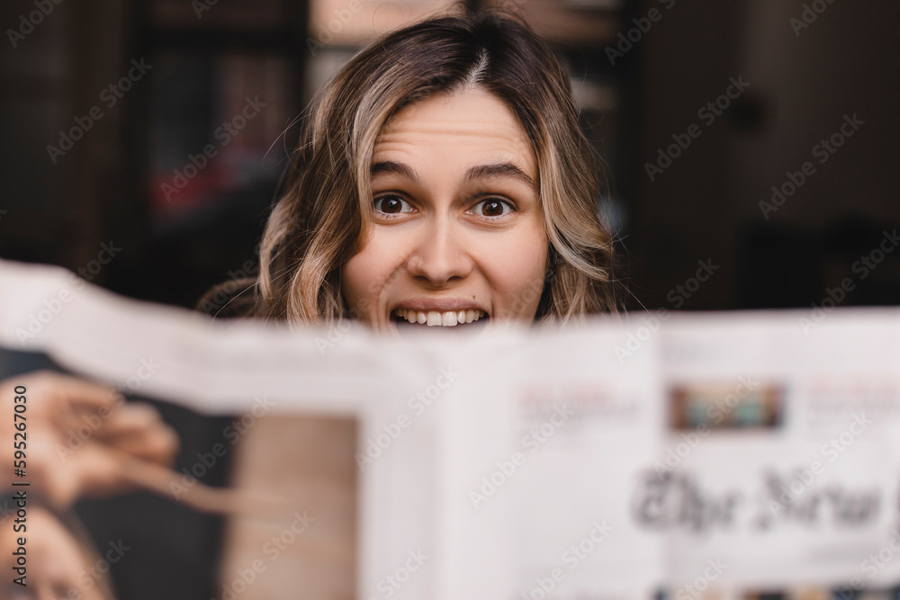 Surprised casual woman reading newspaper and open mouth, laughing while ...