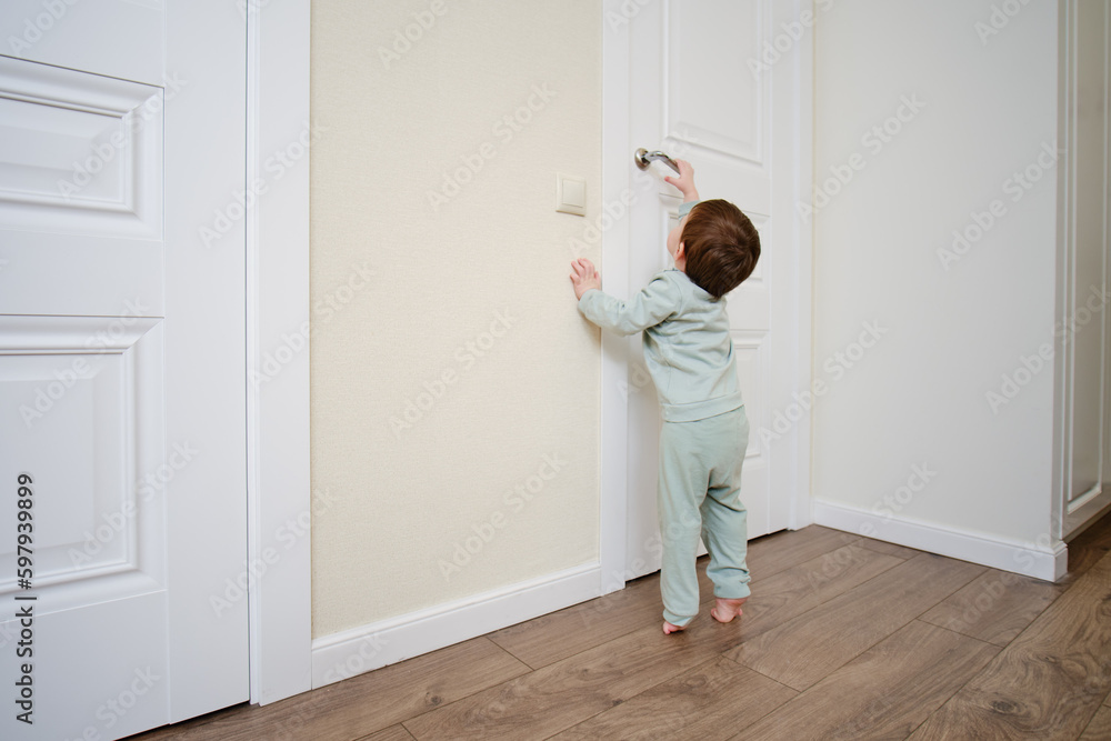 Little baby opens the door. Child pulls the door handle with the lock ...