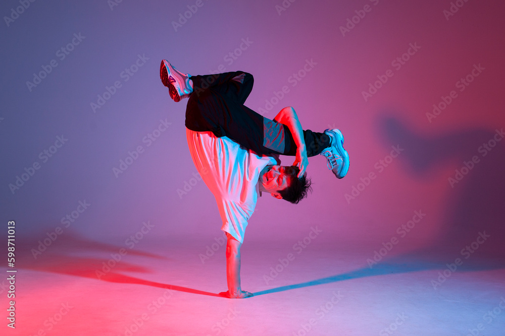 young guy dancer is dancing break in neon lighting, male acrobat is ...