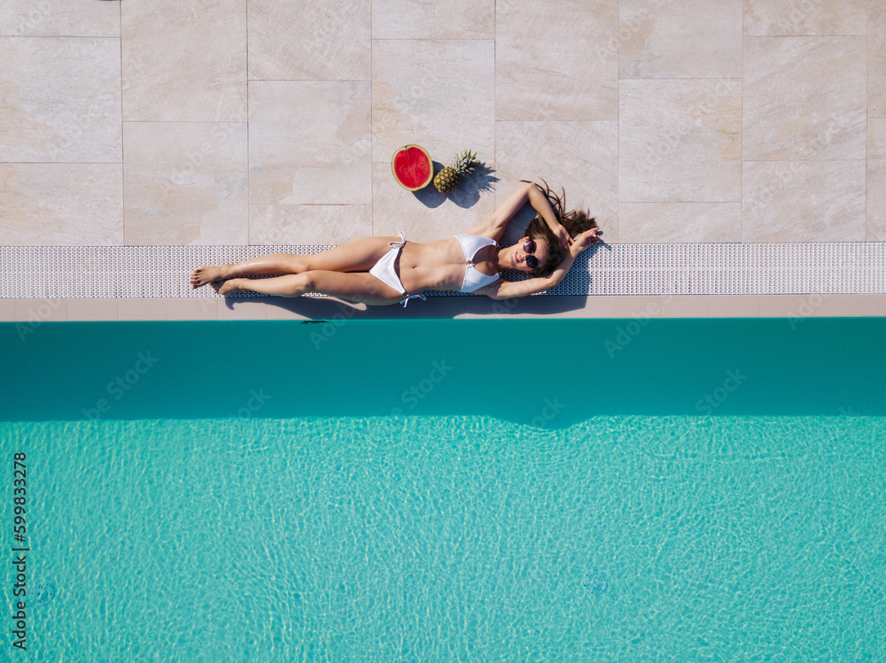 Beautiful sexy woman model in white bikini lies near swimming pool, posing and tanned on summer ...