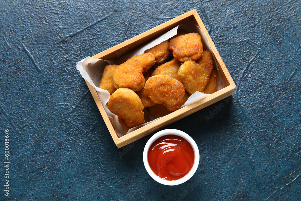 Wooden box with delicious nuggets and bowl of ketchup on dark blue ...