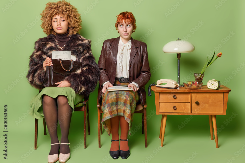 Two women pose on chairs wait for job interview wear fashionable retro ...
