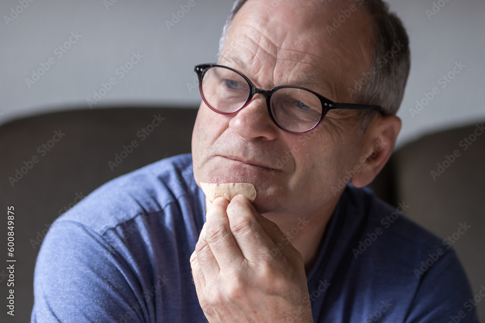 Sad senior man applying sticky medical patch to a wound on his chin ...