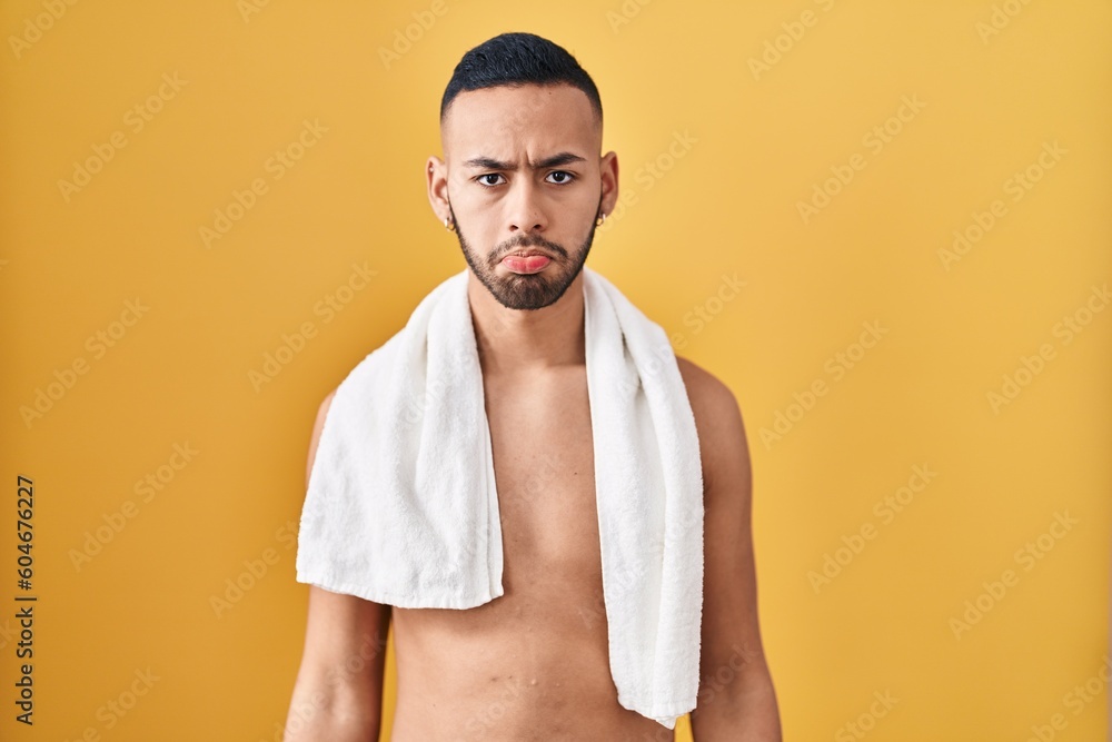 Young hispanic man standing shirtless with towel depressed and worry ...