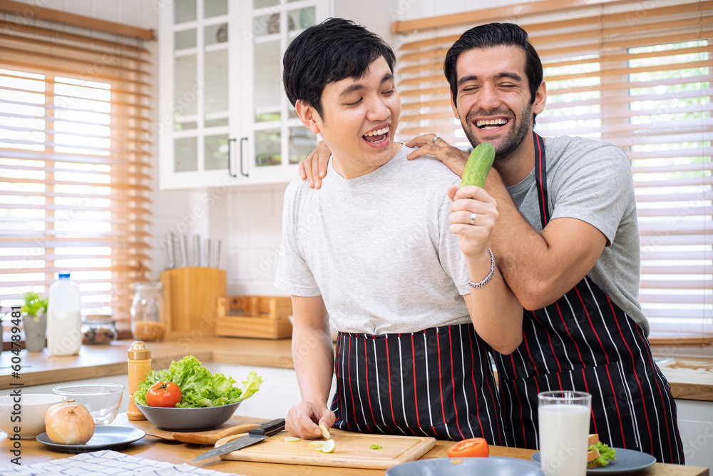 Gay couple teasing each other with cucumbers while cooking in the ...