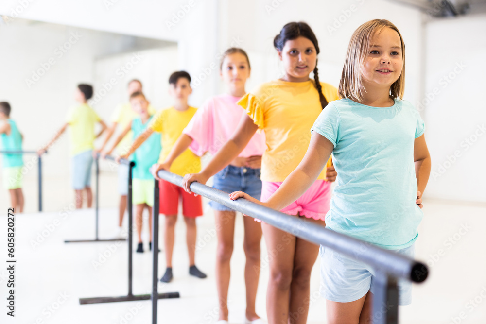 Smiling tween girl practicing classic dance moves near ballet barre ...