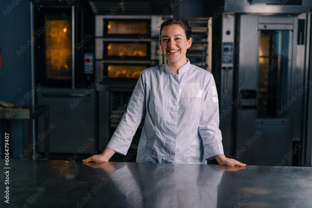 smiling beautiful woman baker in uniform stands near the oven before ...