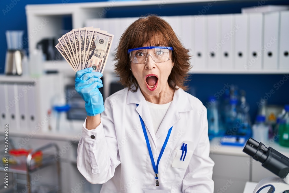 Middle age woman working at scientist laboratory holding money scared ...