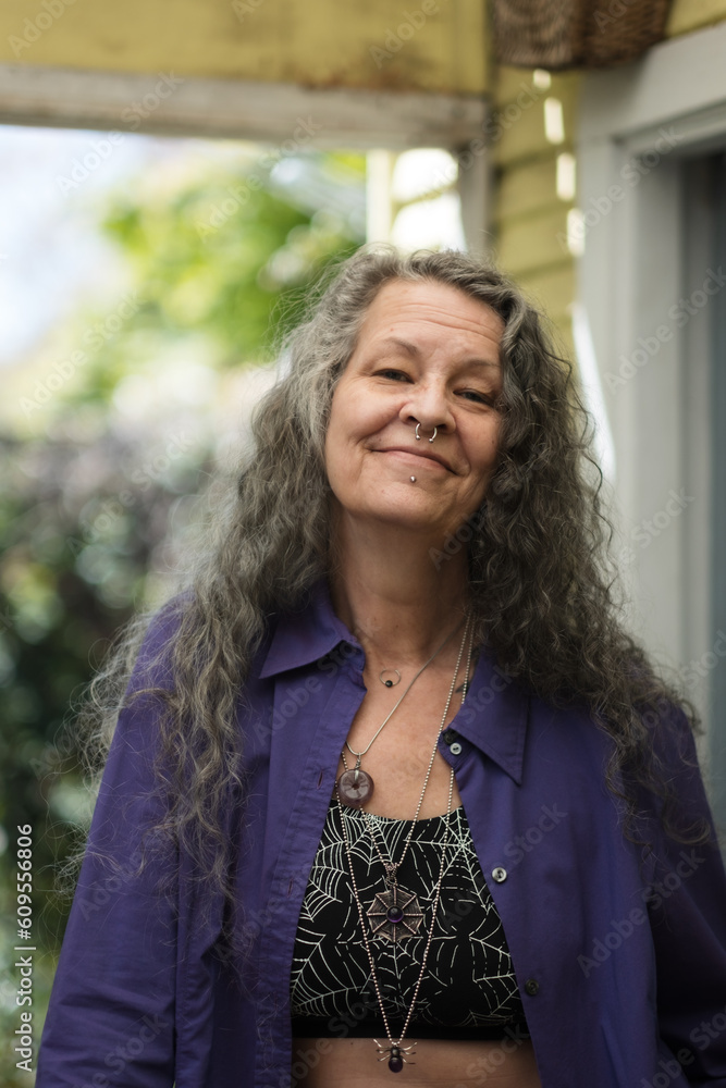 Smiling joyfully, an LGBTQ person poses in their backyard. They have a ...