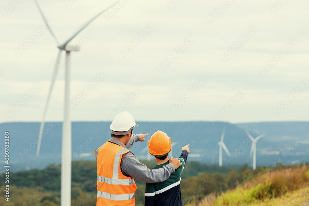 Engineer with his son on a wind farm atop a hill or mountain in the ...