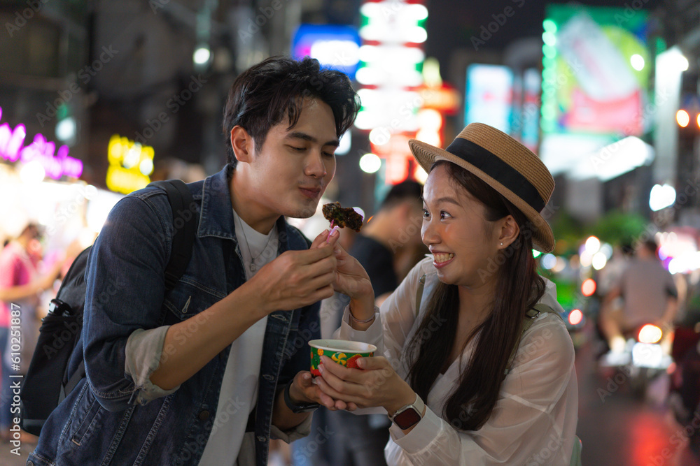 Asian couple tourist backpacker enjoying and eating street food in night market with crowd of ...