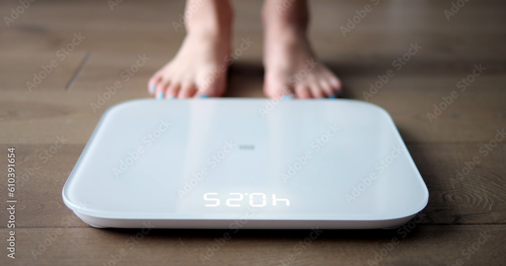 Close-up white scales after weight check and female person feet stand ...