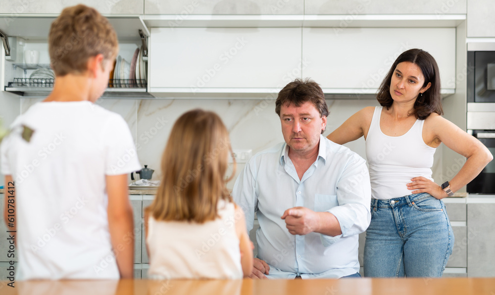 Little brother and sister standing in the kitchen being admonished by ...