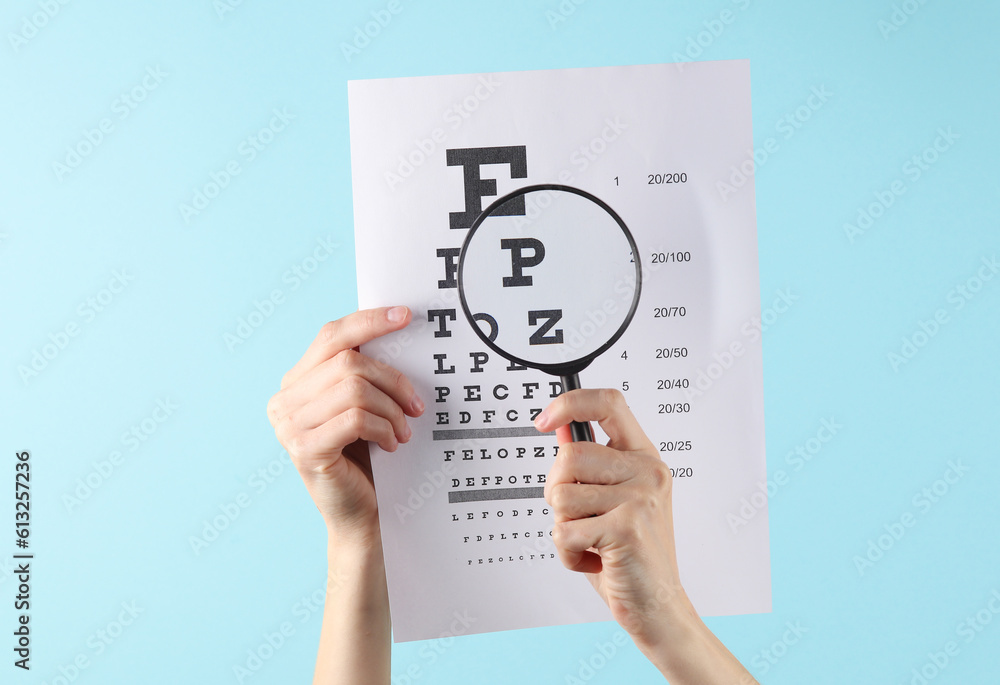 Hands holding eye test chart paper sheet and magnifying glass on blue ...