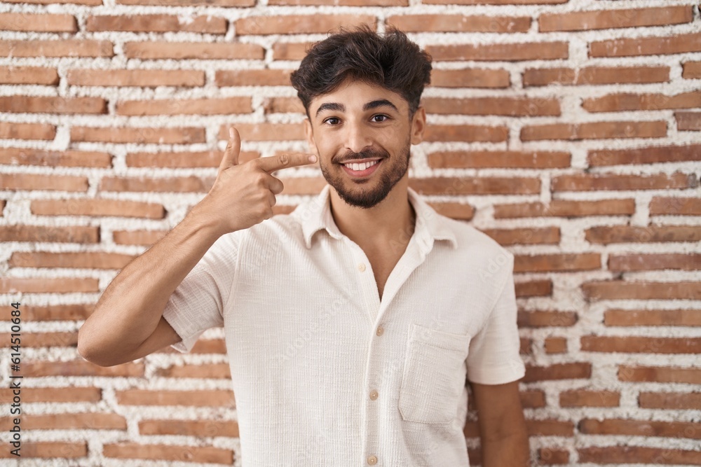 Arab man with beard standing over bricks wall background pointing with ...