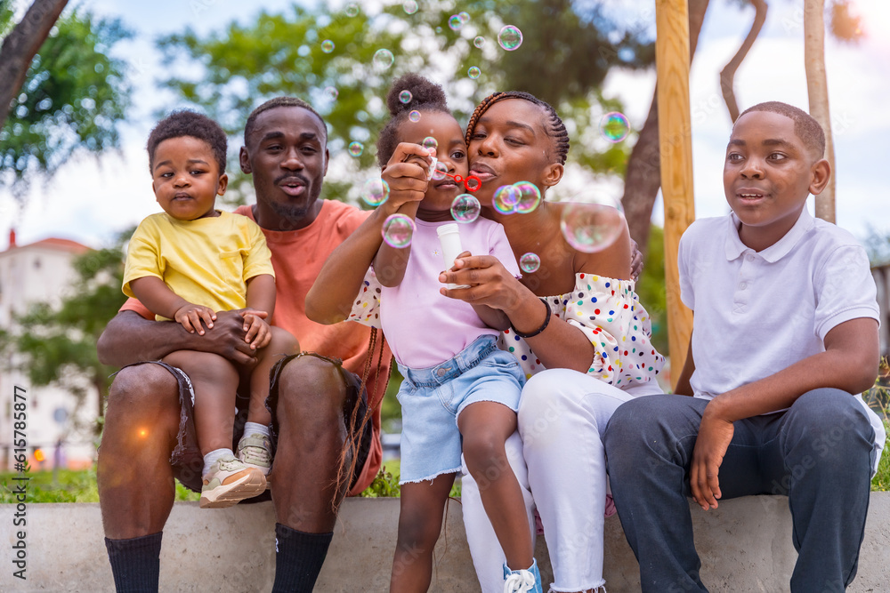 African black ethnic family with children in playground blowing soap ...