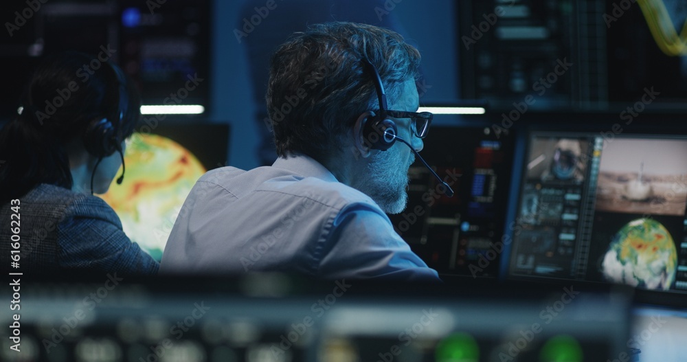 Diverse flight control workers sit in front of computers, monitor space ...