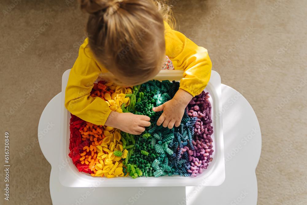 Child playing with sensory bin with dried pasta in rainbow colors. Dyed ...