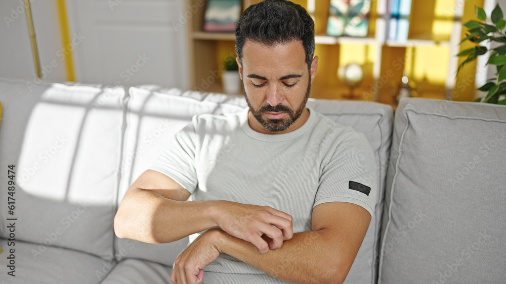 Young hispanic man sitting on sofa scratching arm at home Stock Photo ...