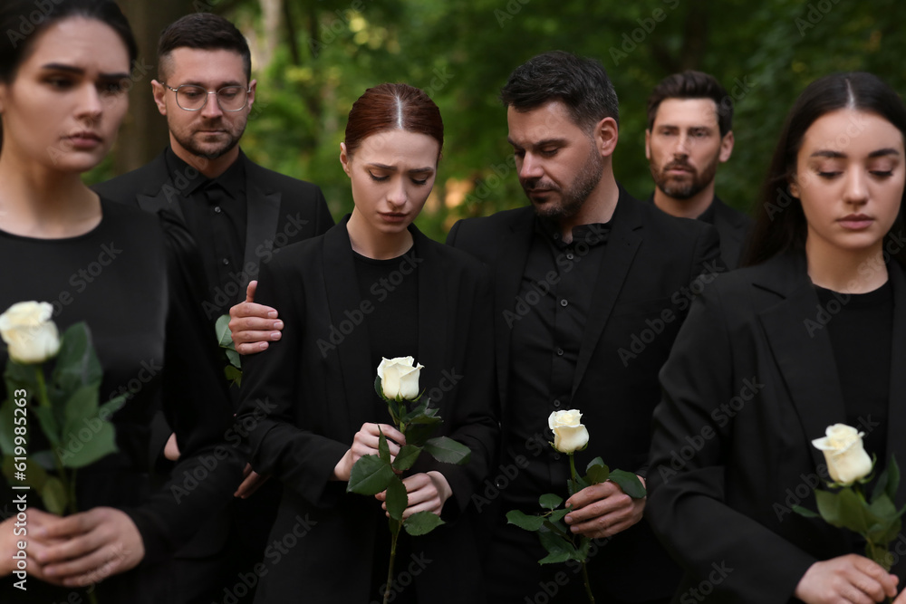 Funeral ceremony. Sad people with white rose flowers mourning outdoors ...
