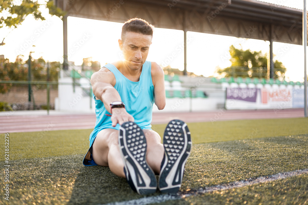 An adult senior soccer player with an amputated arm stretches his legs ...