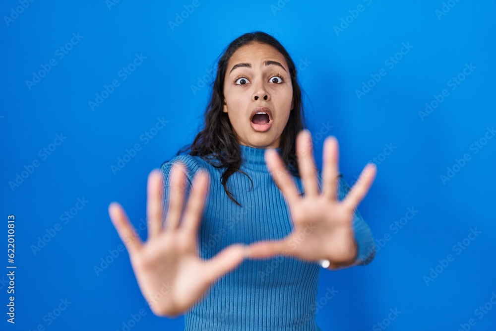 Young brazilian woman standing over blue isolated background afraid and ...