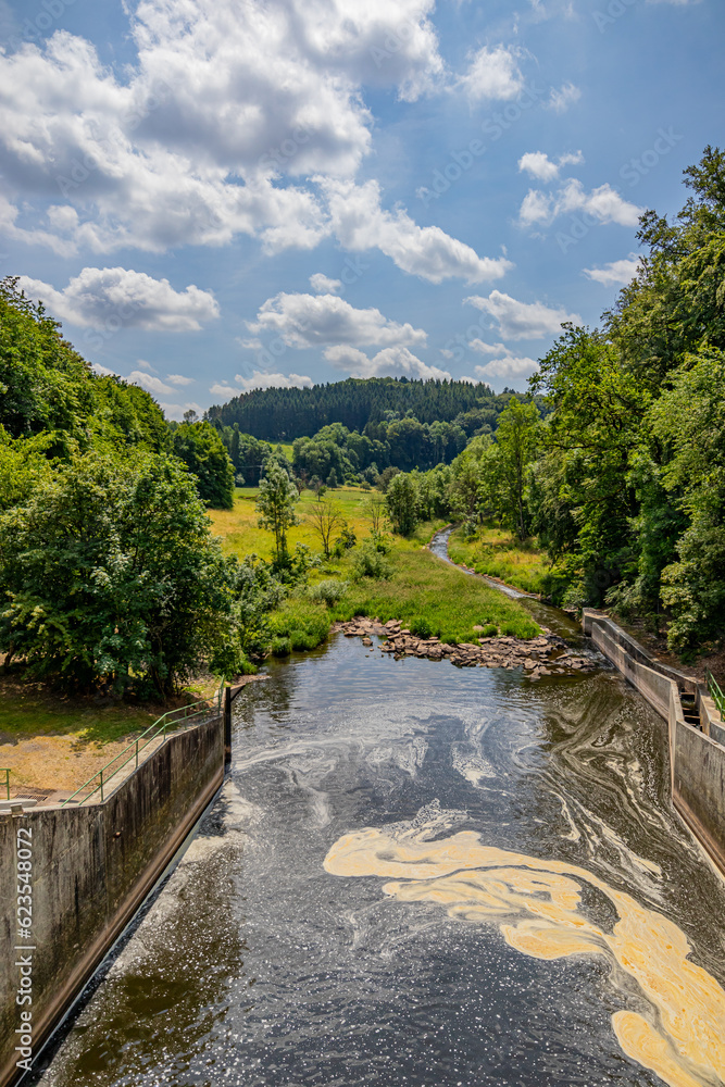 Water flowing out of Staumauer Bitburger dam into Prum river, valley ...