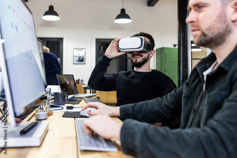 Happy businessman wearing virtual reality simulators with colleague ...
