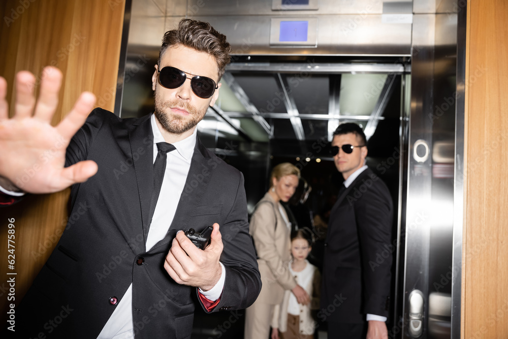 personal safety, handsome bodyguard in sunglasses and suit showing stop ...