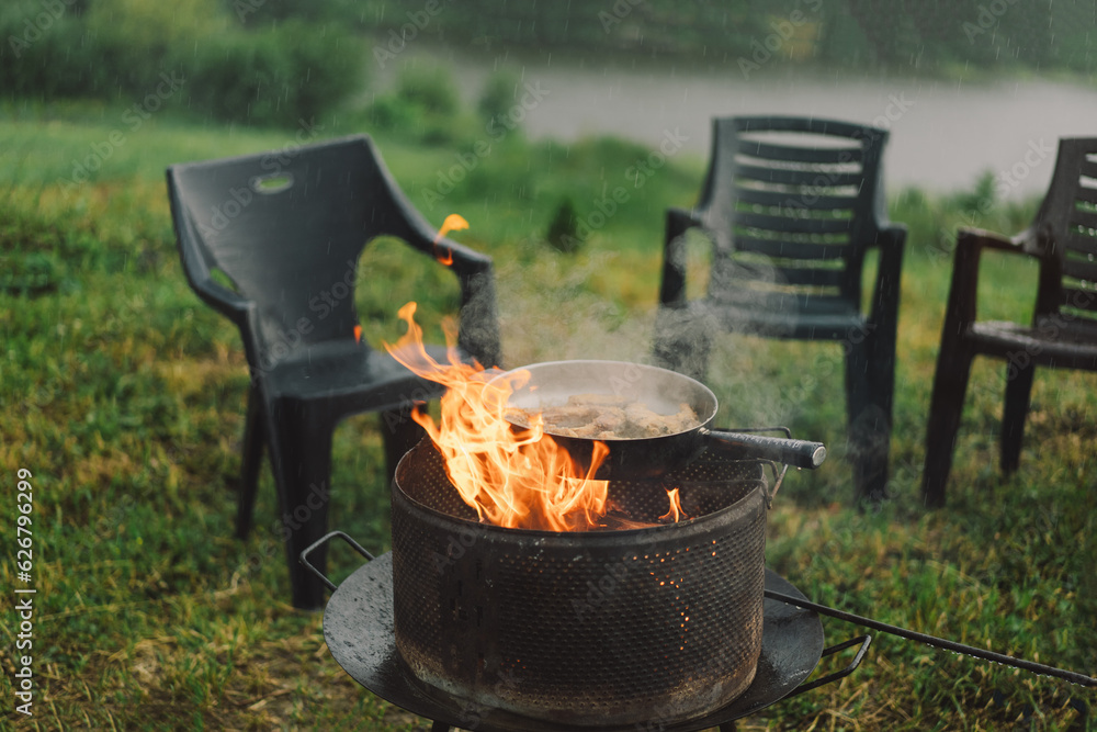 Cooking in the woods outdoors. Man cooking fish on fire in rainy ...