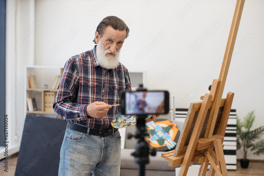 Aged gentleman with long grey beard standing in front of tripod with ...
